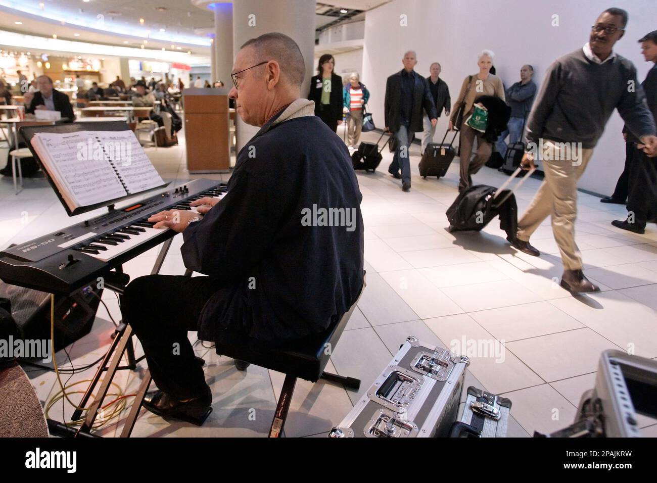 Travelers pass by keyboard player Phil Rugh as he performs in a food ...