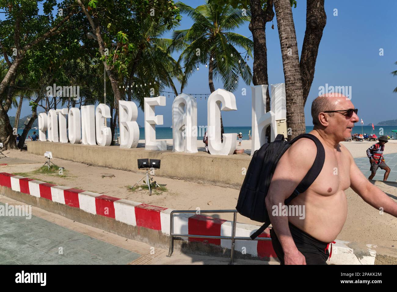 A male Western tourist passes the landmark "Patong Beach" sign, a ...