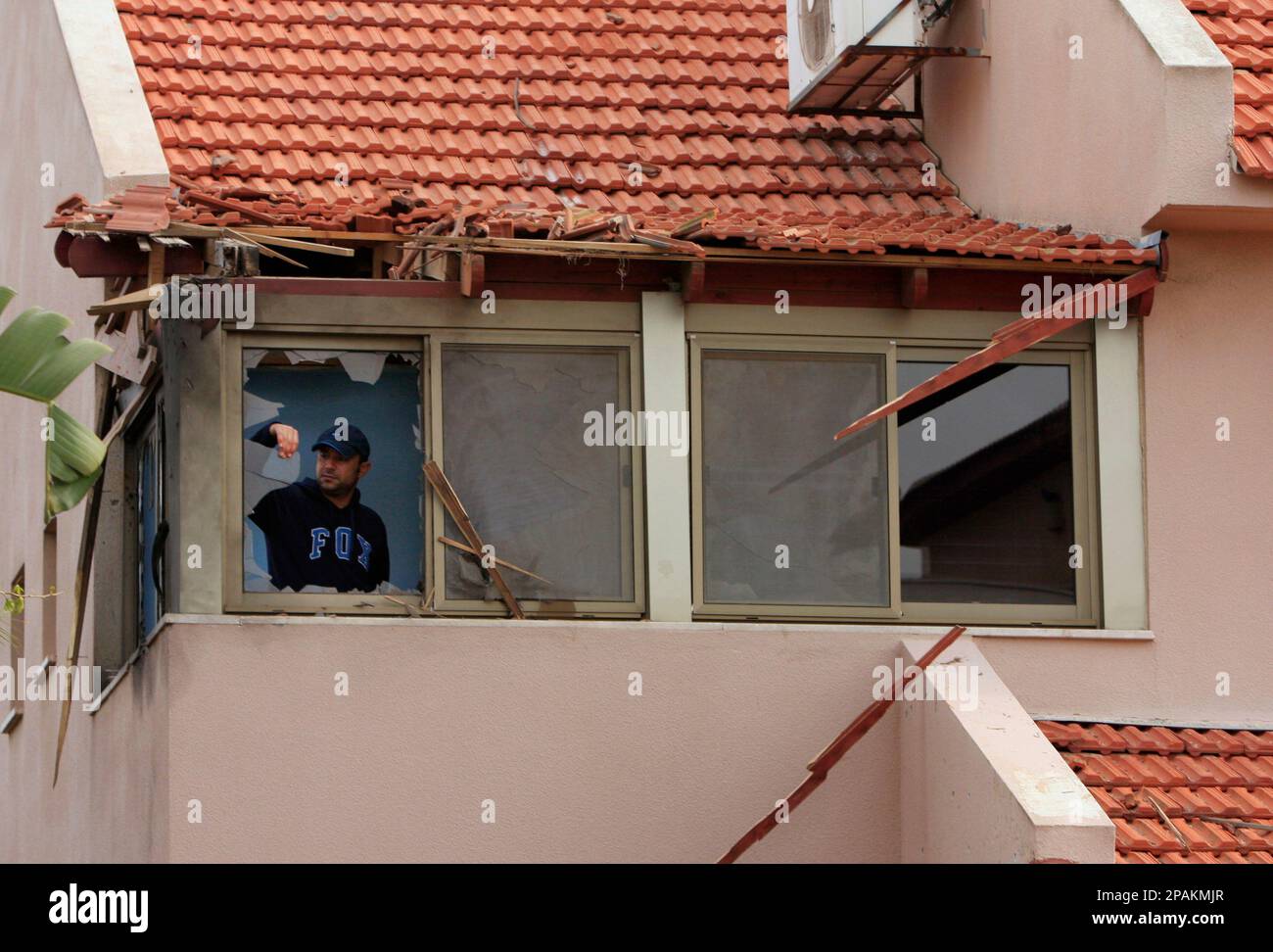 An Israeli man stands in the broken window of a house hit by a rocket ...