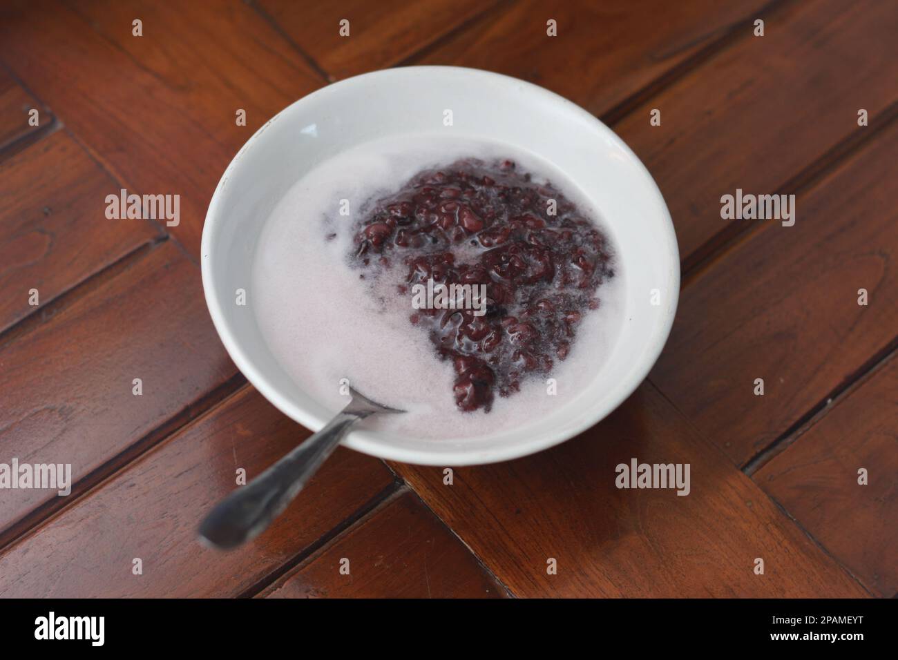 a close up of a bowl of black sticky rice porridge with coconut milk ...