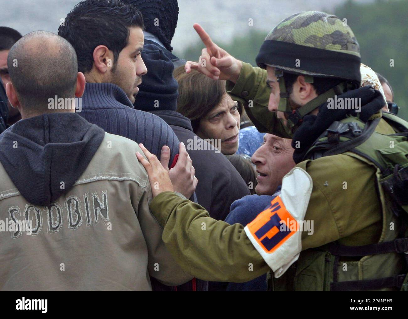 An Israeli soldier gestures as Palestinians wait to cross the Israeli ...
