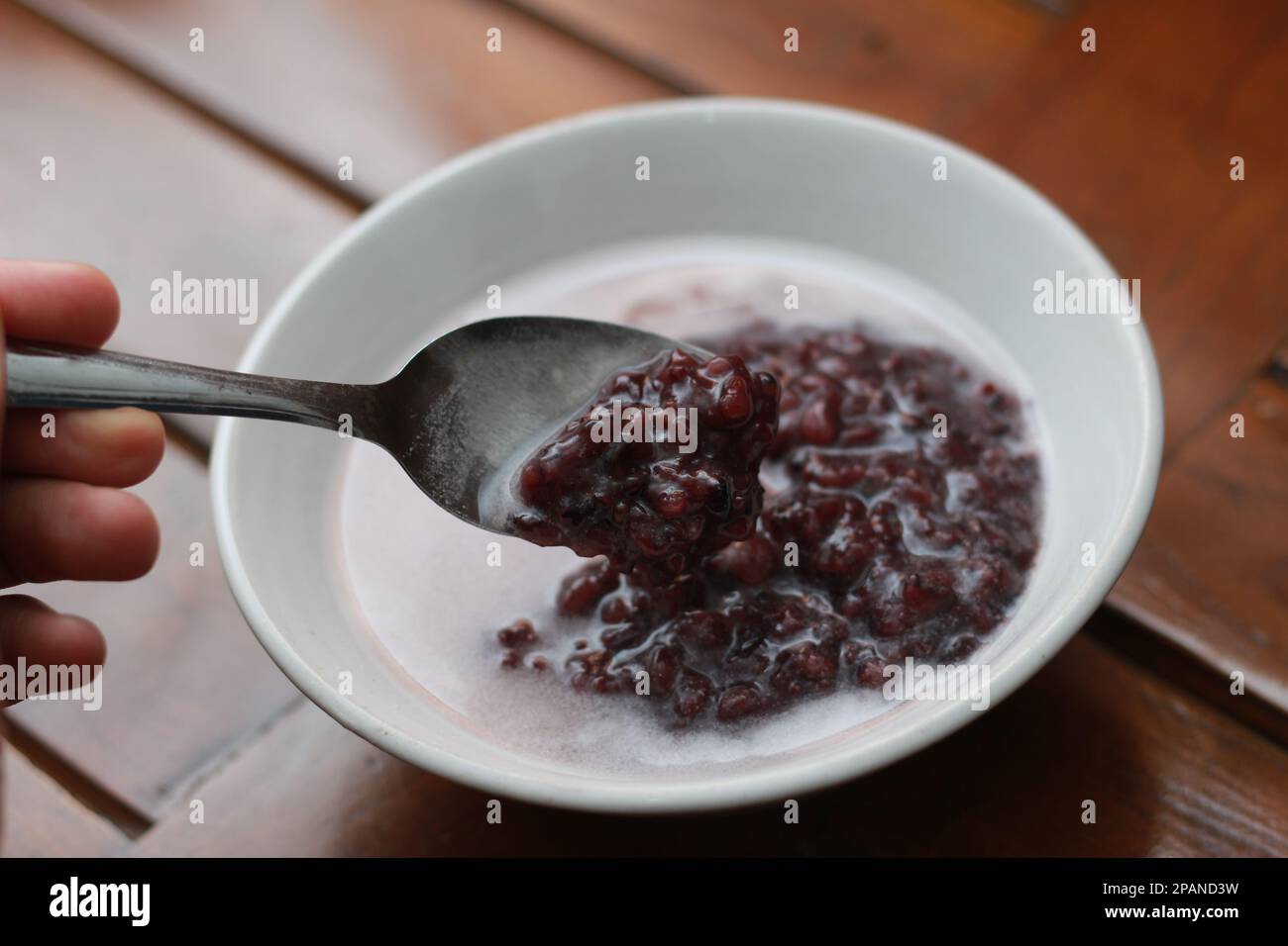 a close up of a bowl of black sticky rice porridge with coconut milk ...