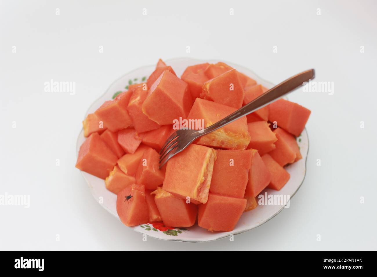 a close up of sliced papaya stabbed with a fork against a blurred ...