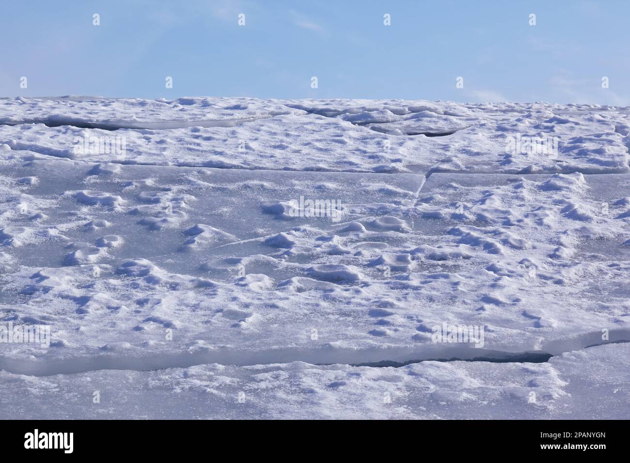 Winter ice landscape under blue sky and clouds. Cracks in the ice field ...