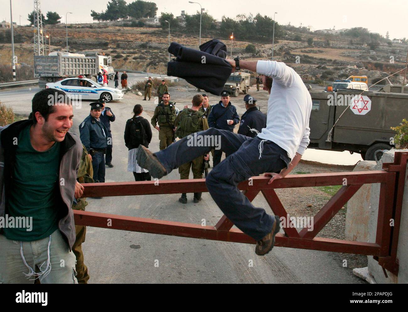 AJewish settler jumps over a barricade past Israeli soldiers at a ...