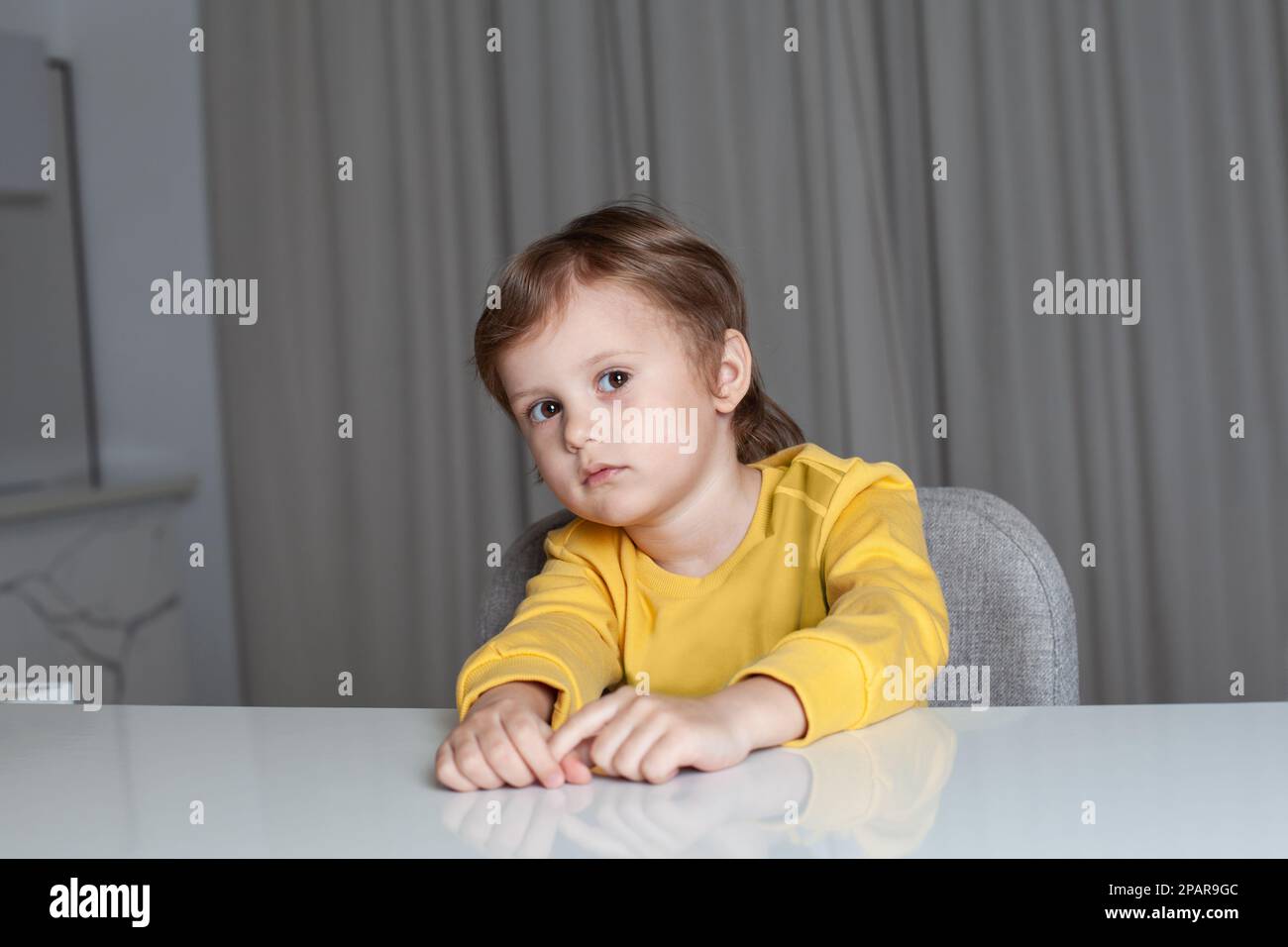 Pensive child boy with brown hair in yellow sweater sitting by the ...