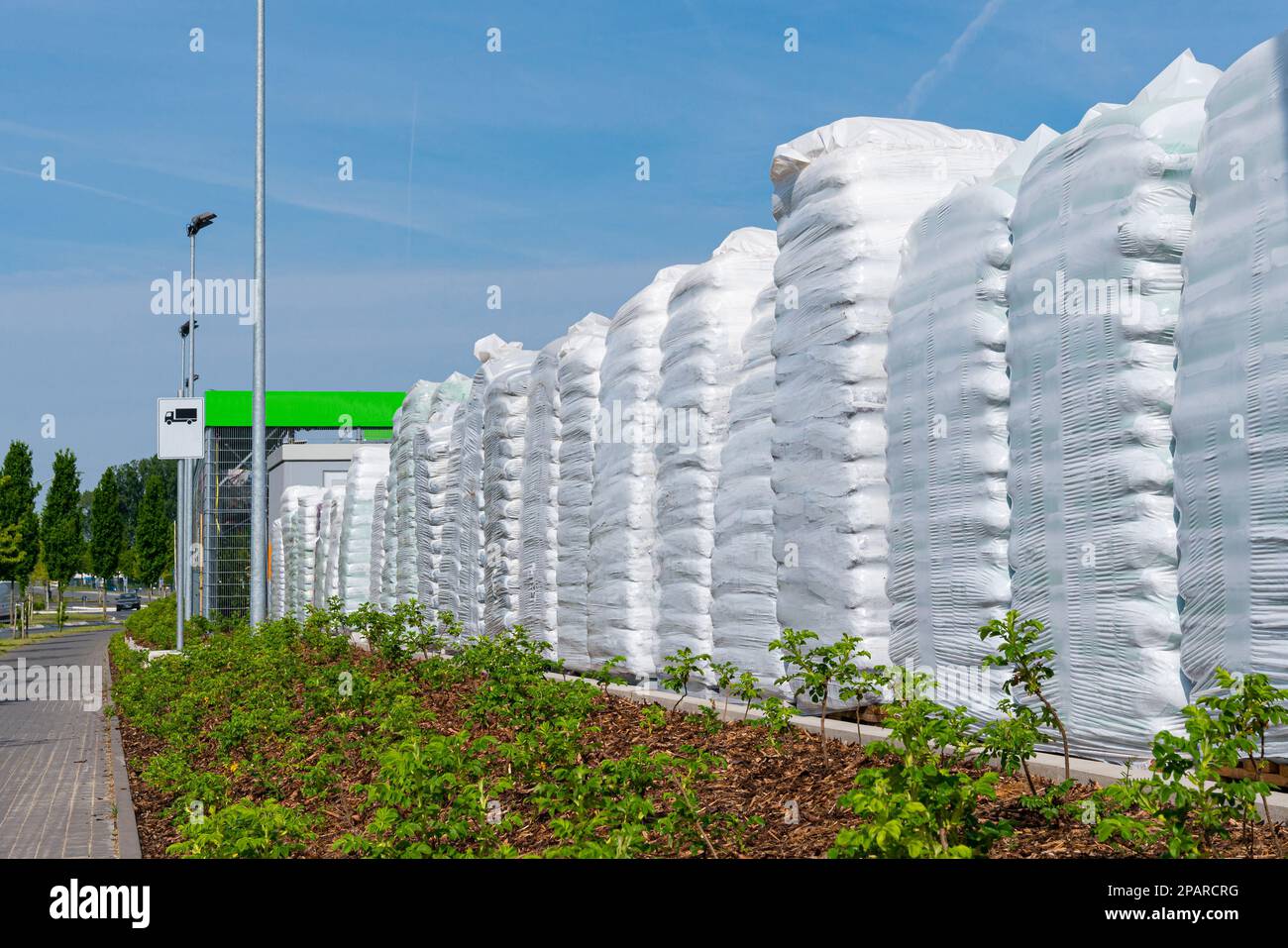 Pile of white plastic sacks stacked along the sidewalk. Blue sky with ...