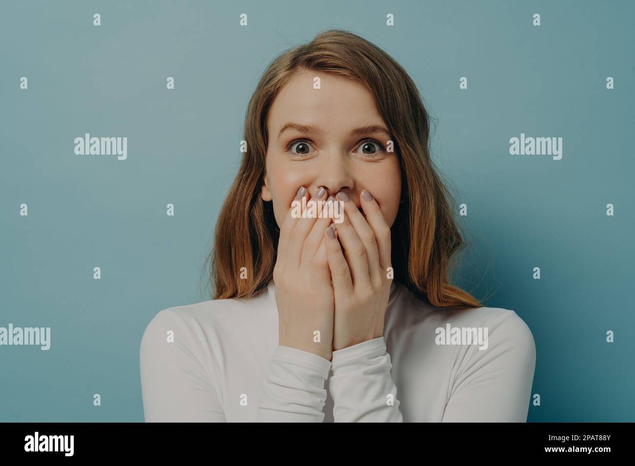 Charming surprised positive young woman closed her mouth with both ...