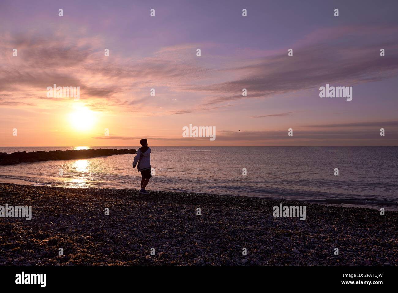Boy playing pebble throwing on the beach at dawn. Unrecognisable, small ...