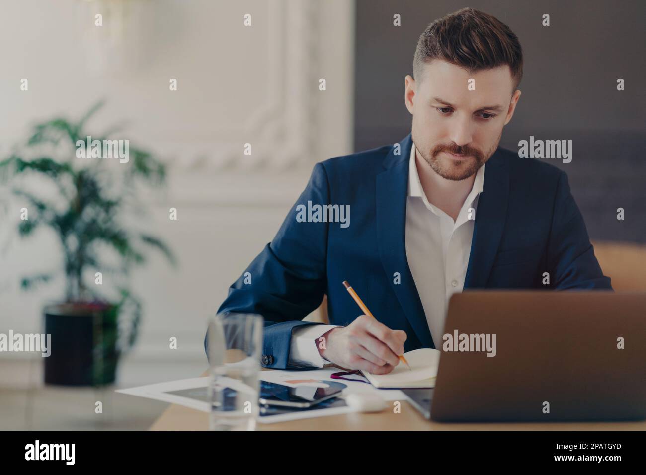 Successful attractive businessman in formal dark blue suit writing down ...