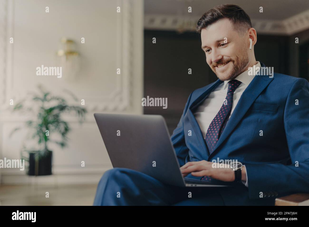 Cheerful unshaven prosperous male entrepreneur works on laptop computer ...