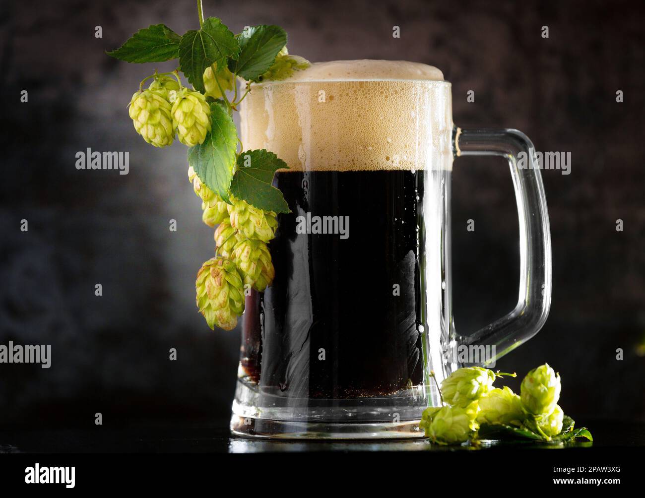 dark beer in a mug and green hop on wooden table on brown background ...