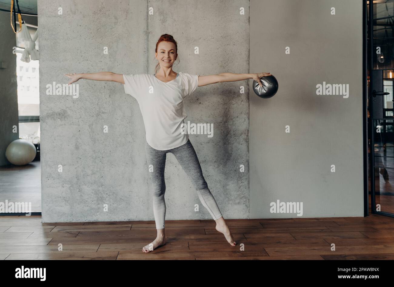 Beautiful healthy ginger woman performing barre exercises with small ...