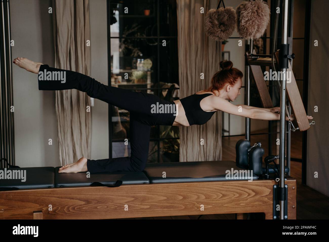 Side view of young athletic woman stretching legs on pilates machine or ...