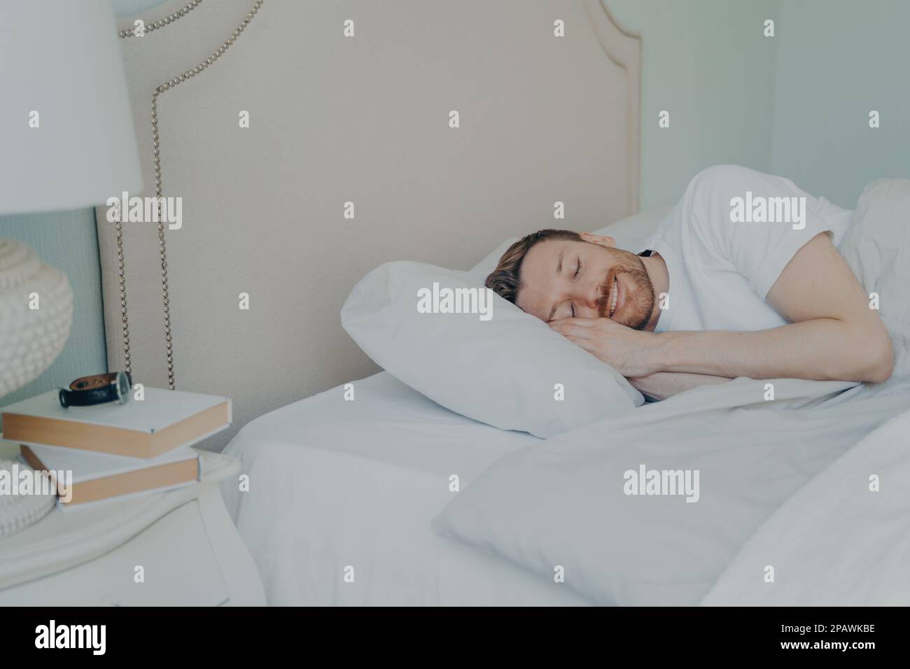 Young relaxed bearded man in casual pajama lying in bed with closed ...