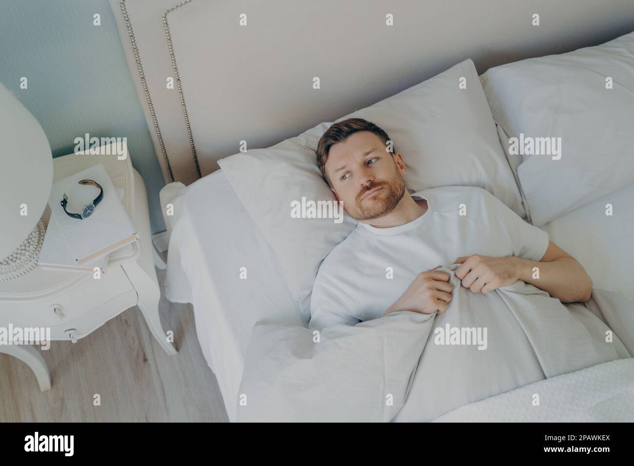 View from above of stressed young caucasian male lying in bed with his ...