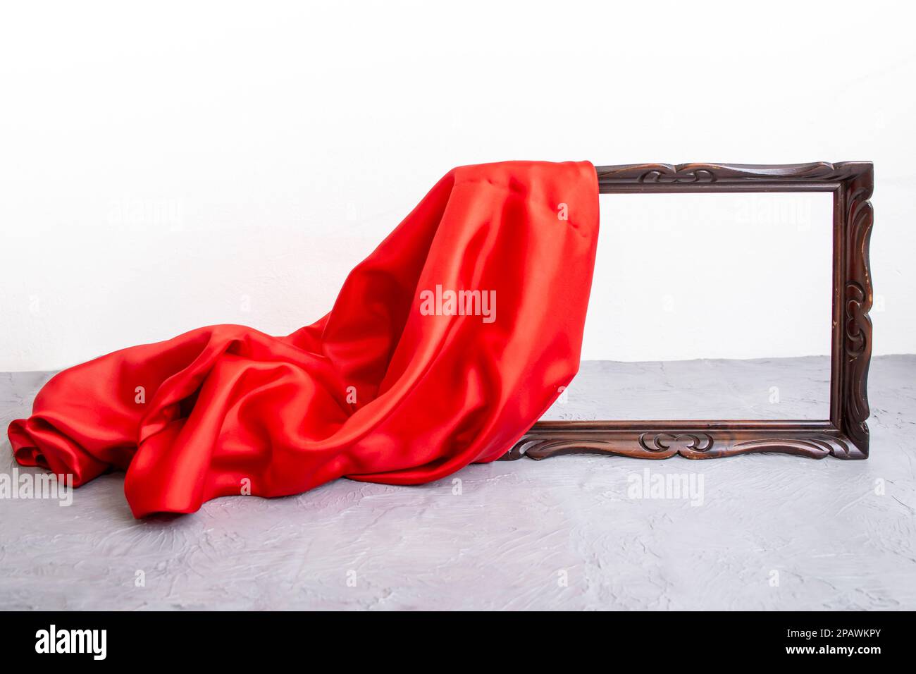 Red satin cloth unveiling a wooden brown frame, on cement table top and ...
