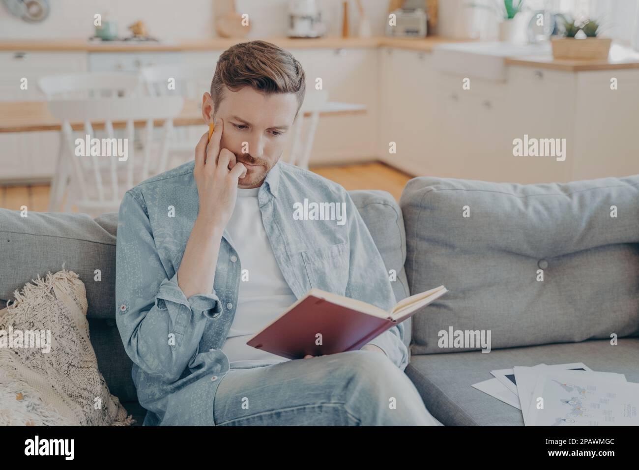 Young handsome man with hand on his face holding pencil, red note book ...