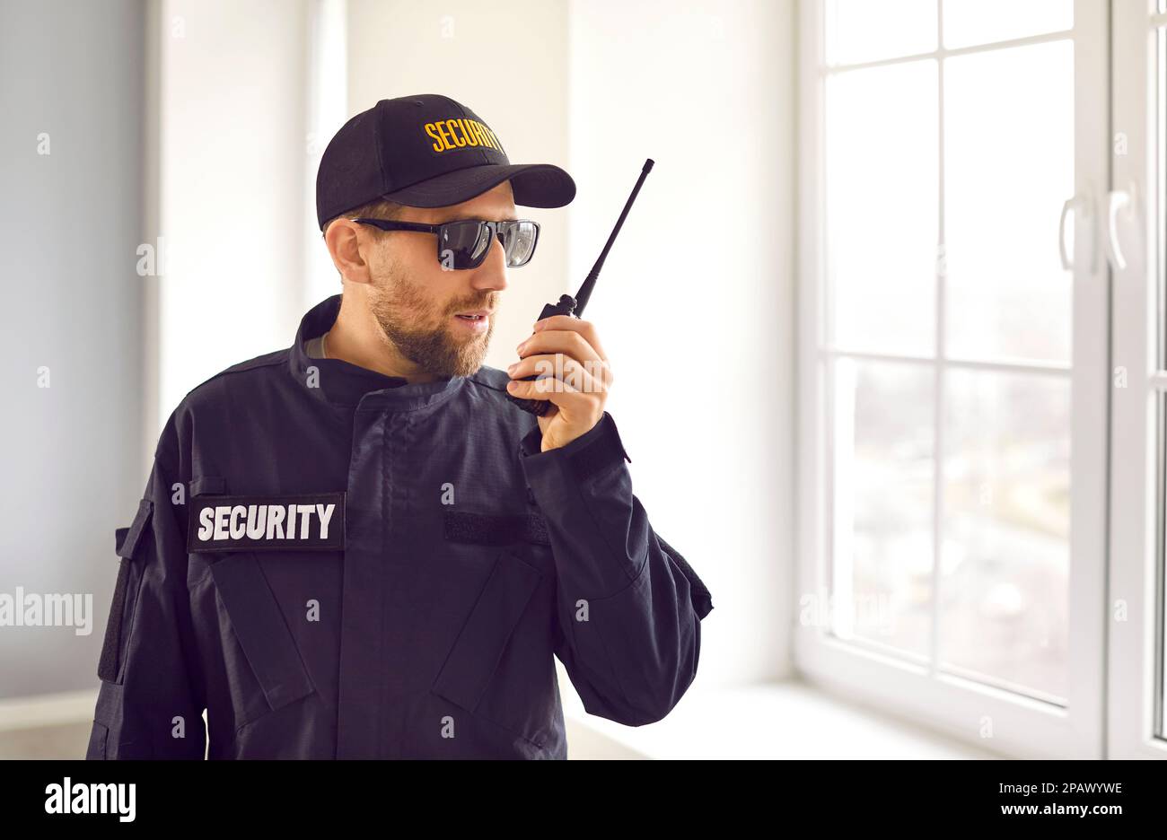 Security guard in uniform standing inside house, looking out window ...