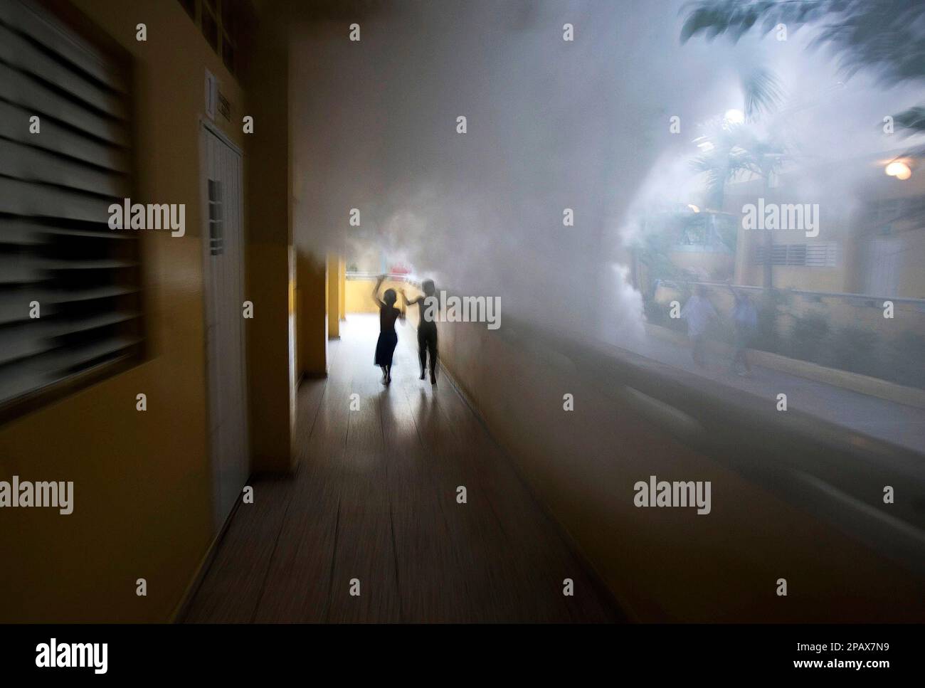 Children play as a truck sprays insecticide in a school being used as a ...