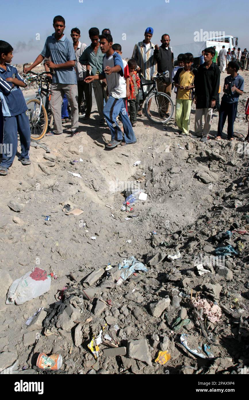 People gather around a crater left by a roadside bomb explosion in ...