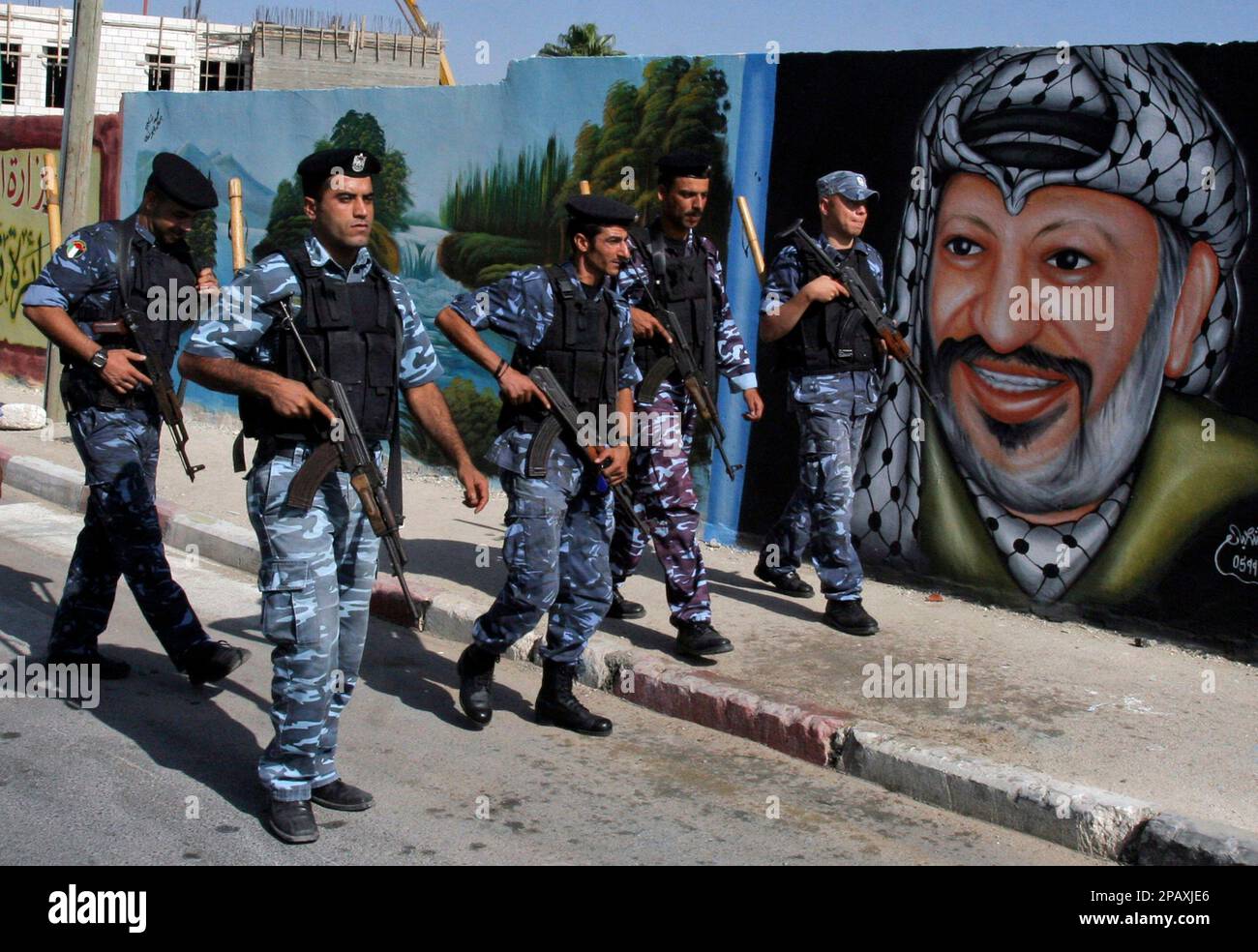 Palestinian police officers walk next to a mural depicting late ...