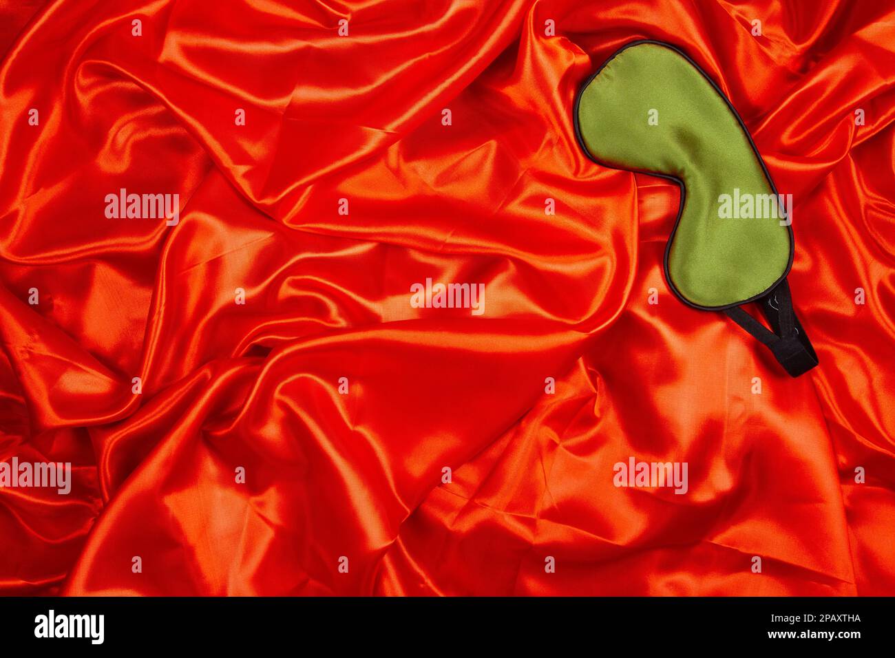 Green silk sleep mask lie on bright red silken background. Horizontal ...