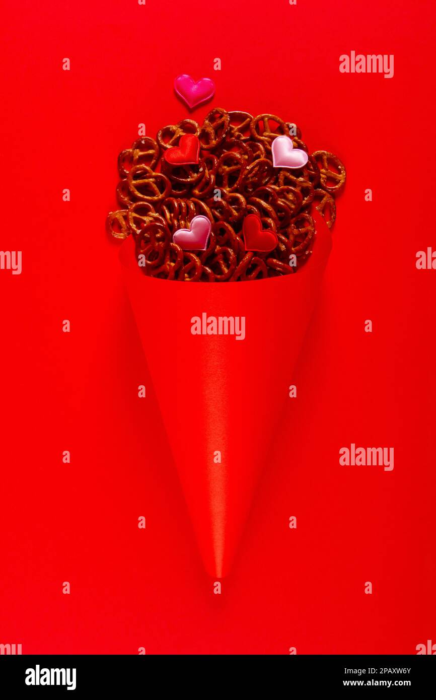Mini pretzels and small colorful hearts in red paper cone lie on red ...