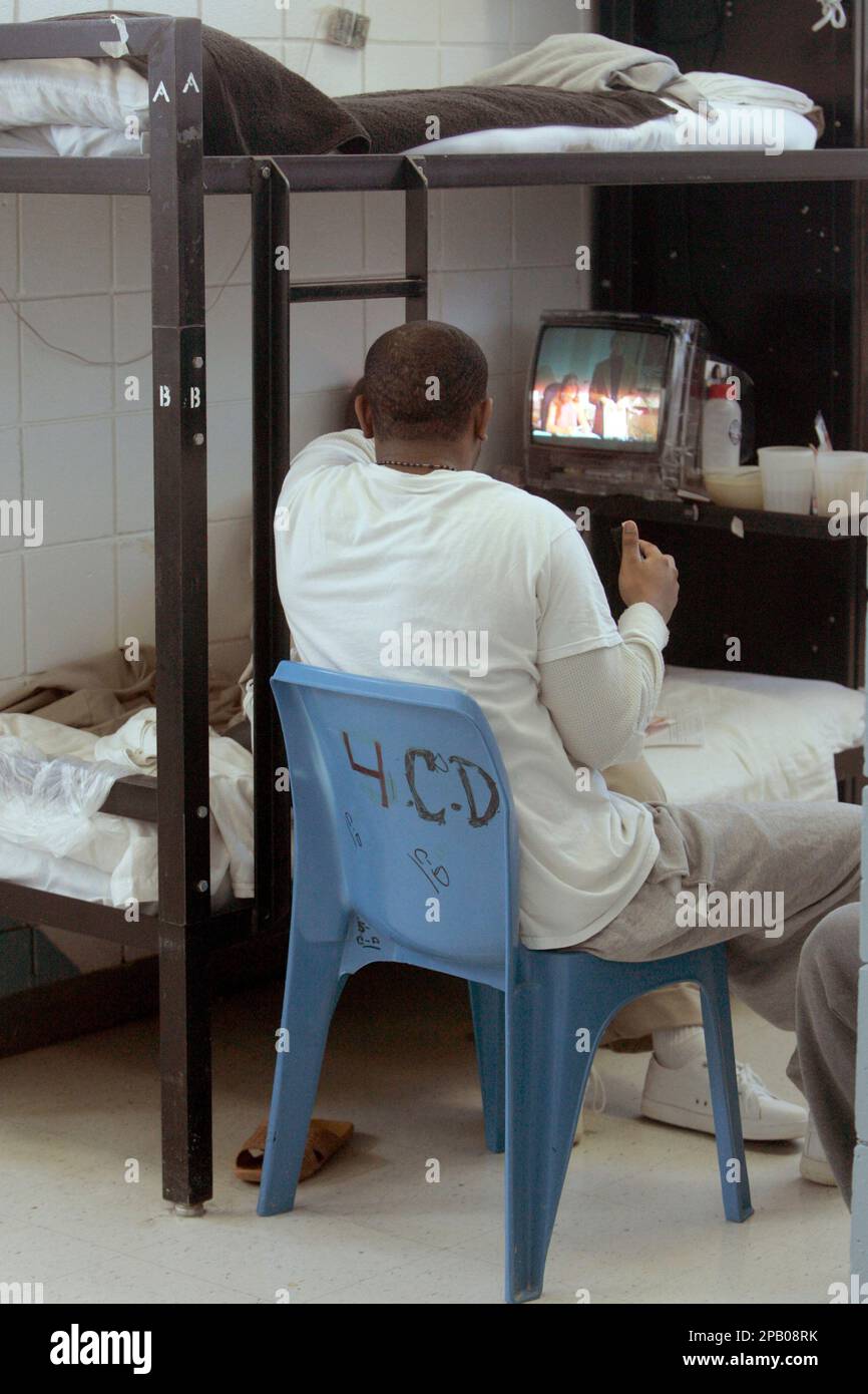 An inmate sits on a chair next to the double-decker bunk in a cubicle ...