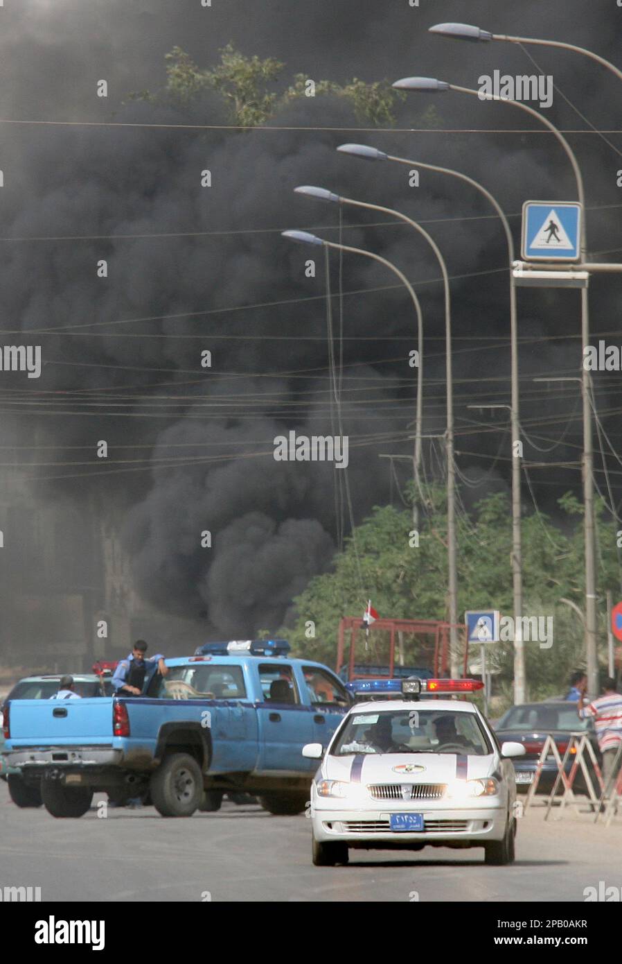 An Iraqi police car drives near the scene, as smoke rises into the sky ...