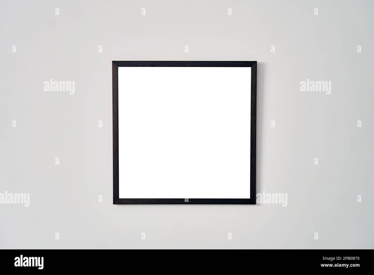 An empty square photo frame with a black border hanging on a white wall ...