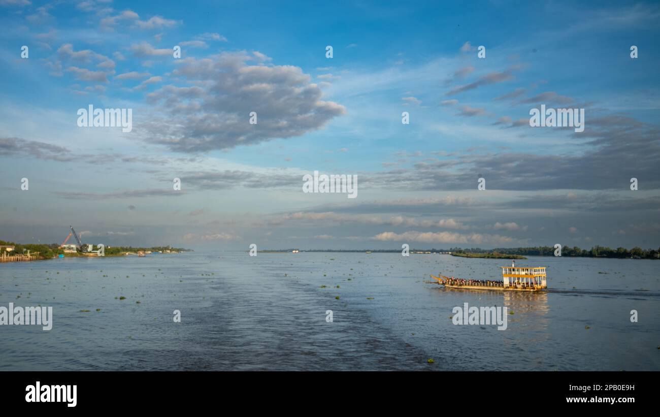 A crowded river ferryboat crosses the Mekong River just after dawn ...