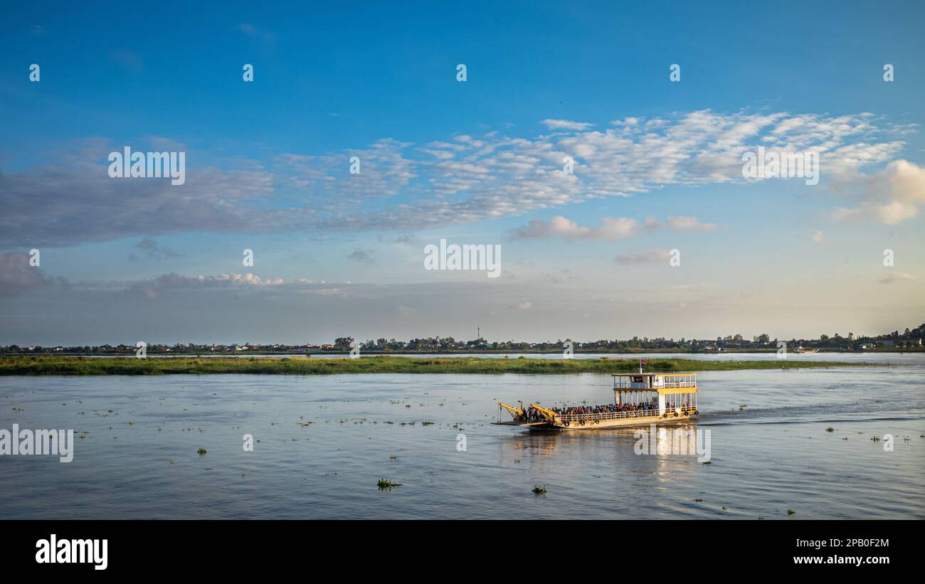 A crowded river ferryboat crosses the Mekong River just after dawn ...