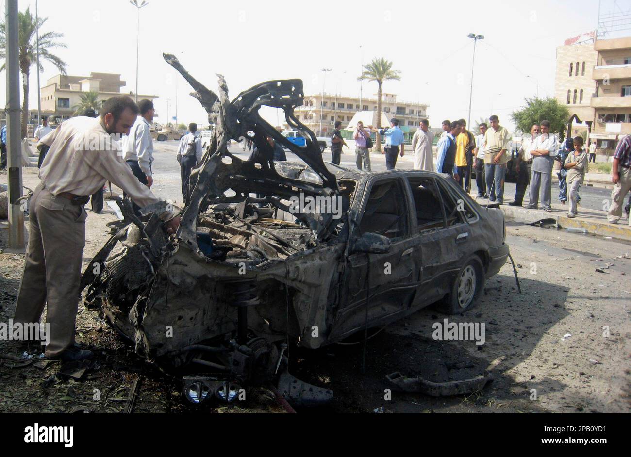Iraqi men inspect a damaged car after a car bomb attack in Saddam ...