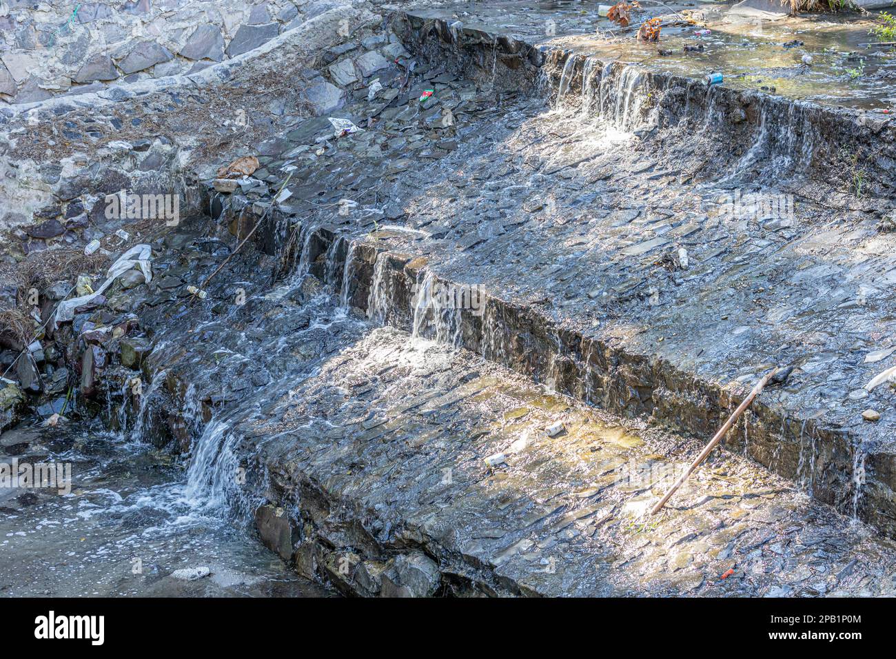 Open sewage stone channel with a spillway with garbage on the ...