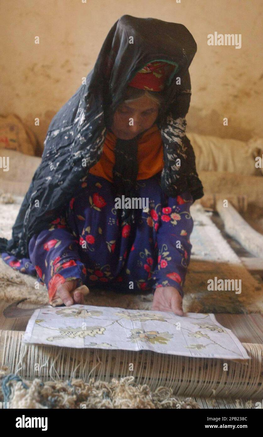 An Afghan elderly woman checks a design, as she works on a carpet in ...