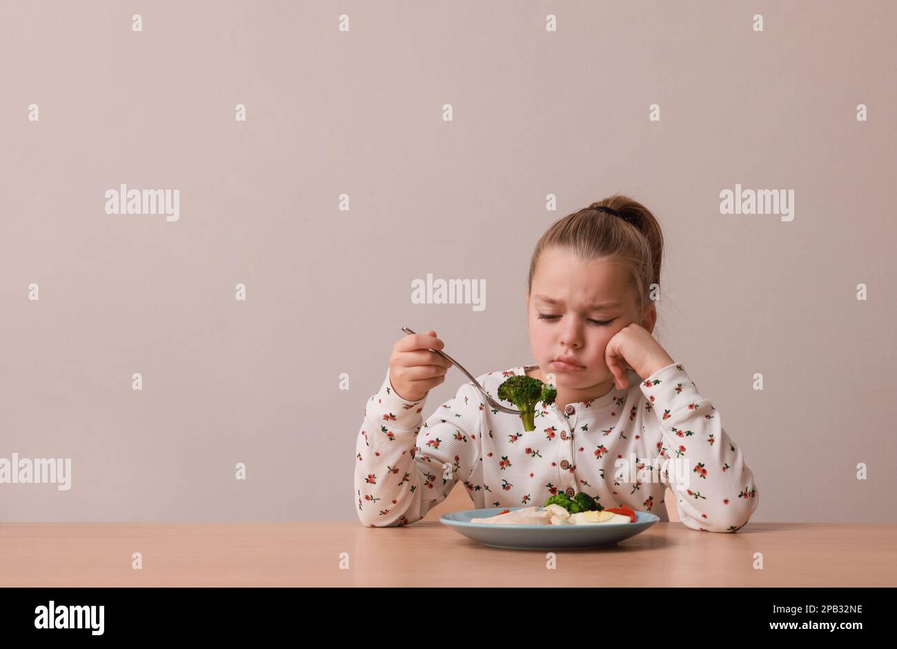Cute little girl refusing to eat her dinner at table on grey background ...