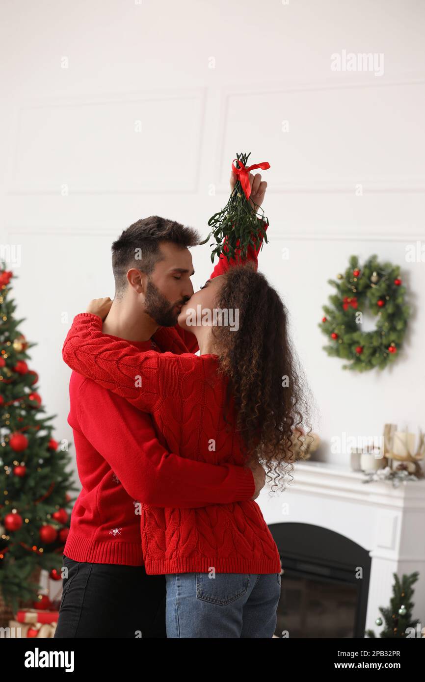 Happy couple kissing under mistletoe bunch in room decorated for ...