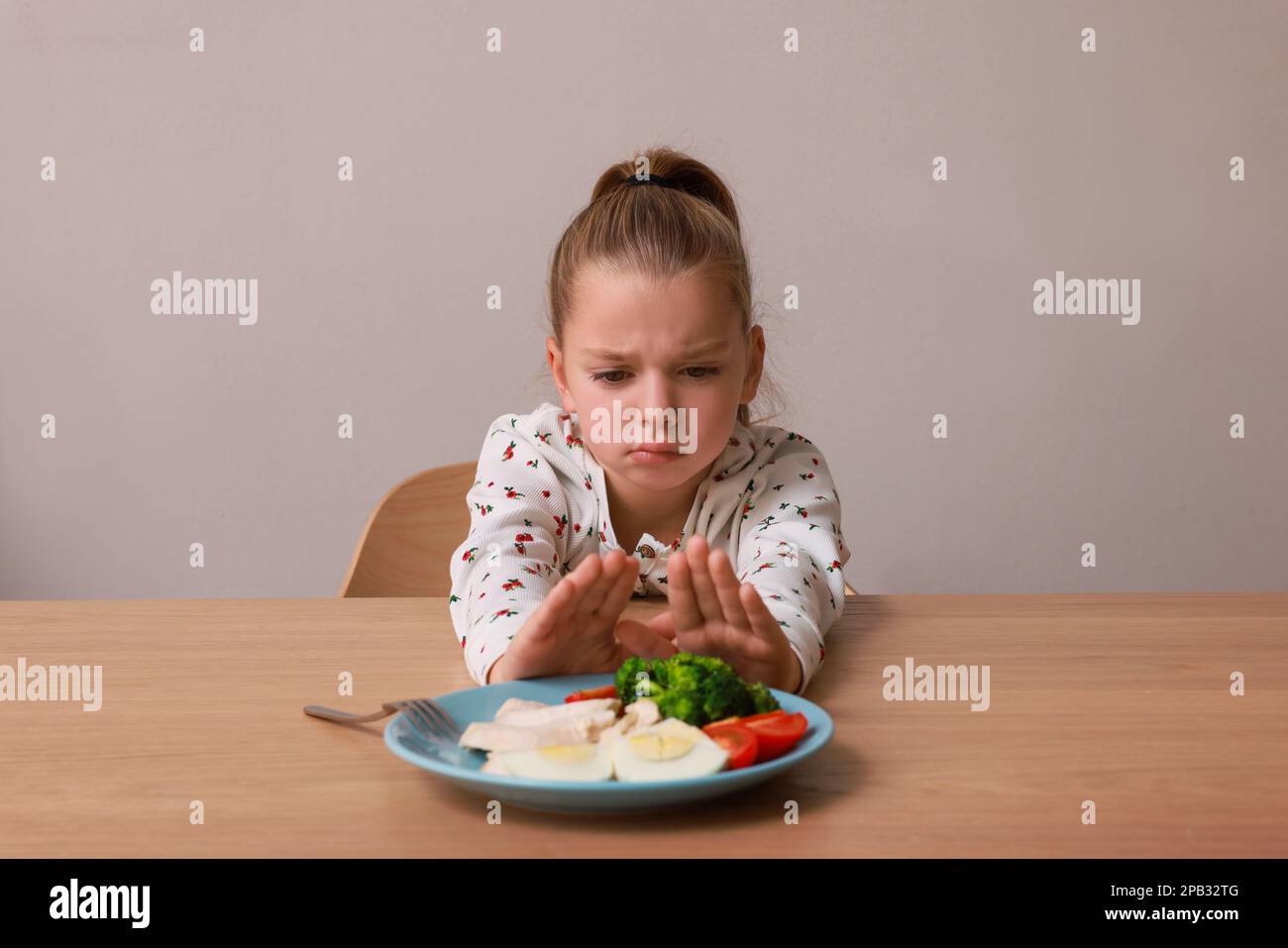 Cute little girl refusing to eat her dinner at table on grey background ...