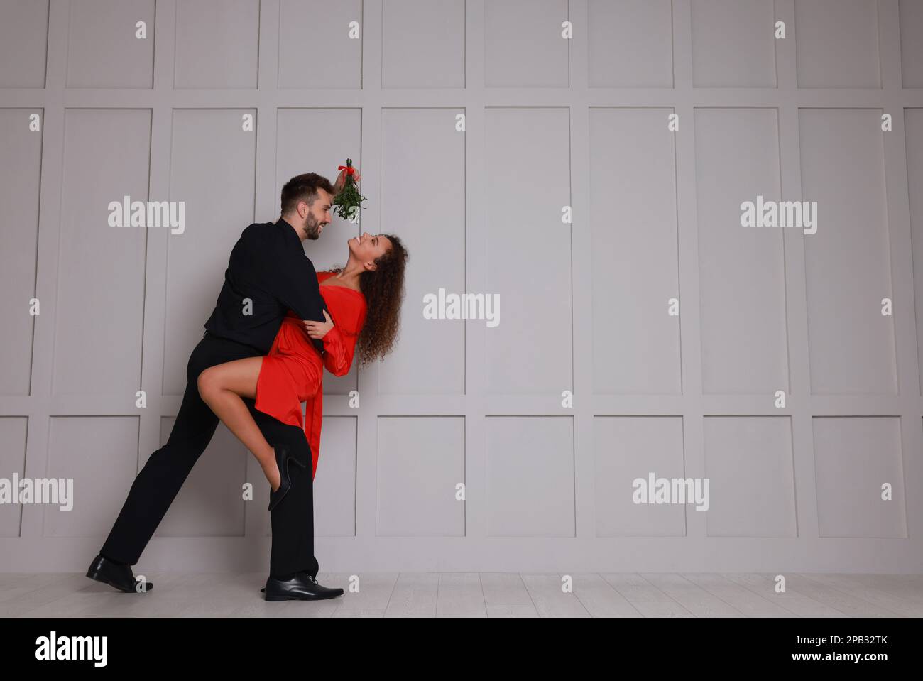 Lovely couple dancing under mistletoe bunch near light grey wall. Space ...