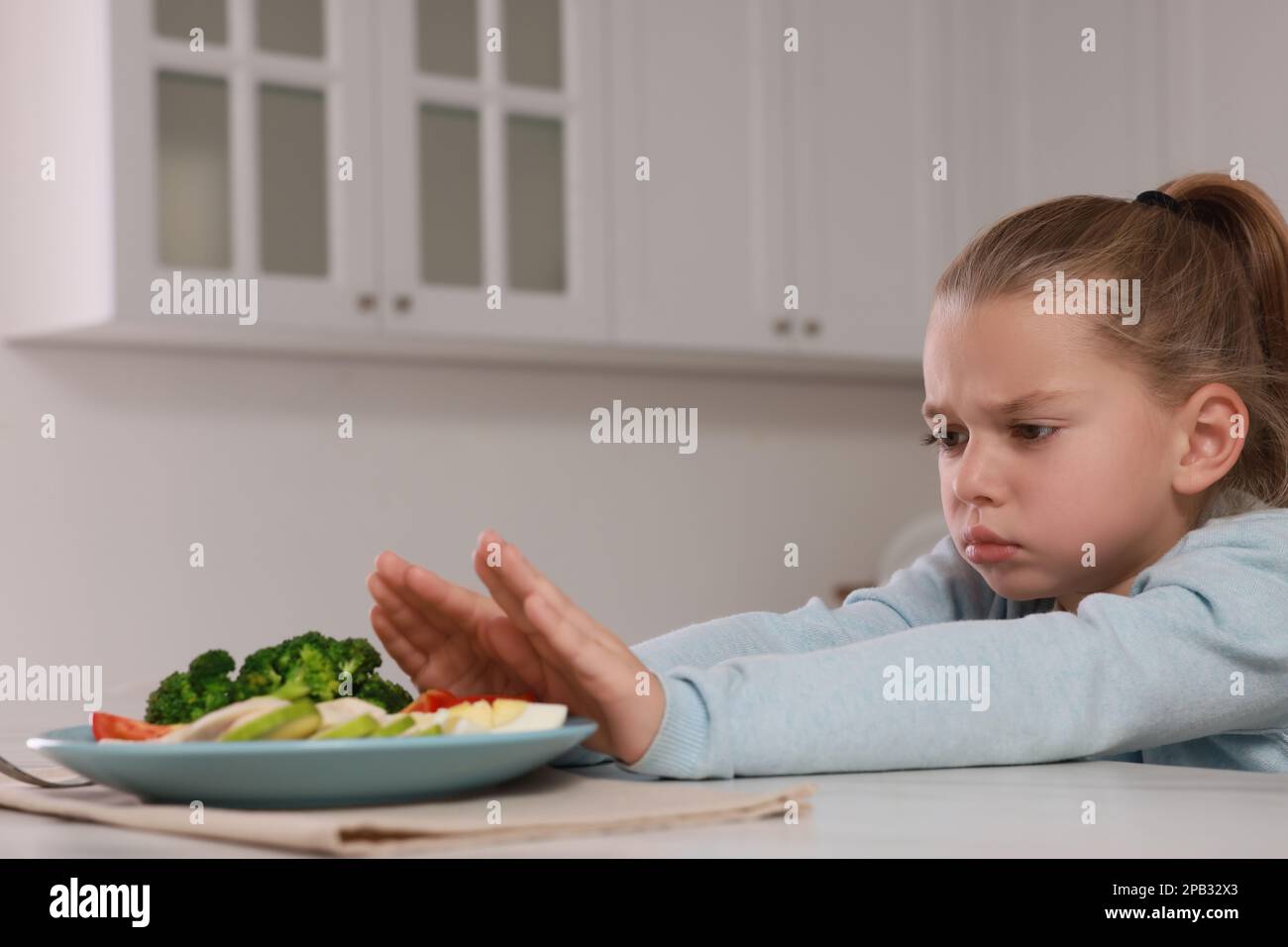 Cute little girl refusing to eat dinner in kitchen, space for text ...
