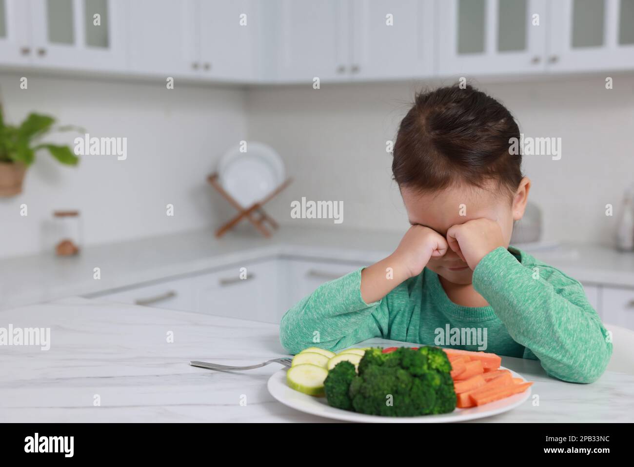 Cute little girl crying and refusing to eat vegetables in kitchen ...