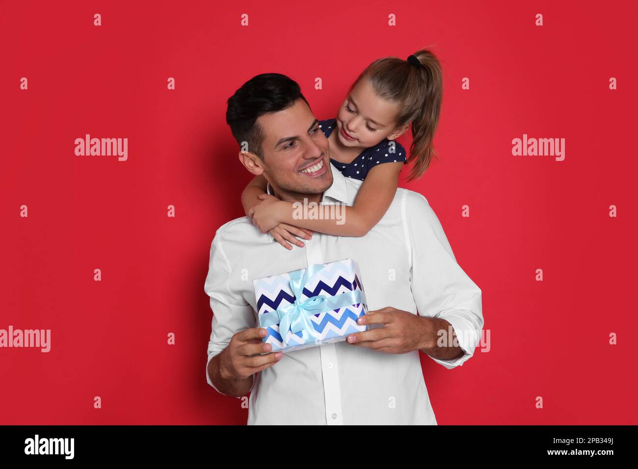 Man receiving gift for Father's Day from his daughter on red background ...