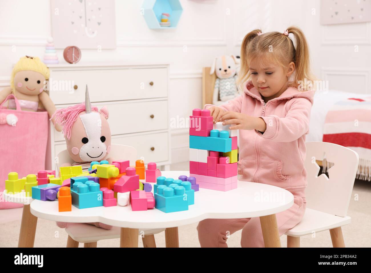Cute little girl playing with colorful building blocks at table in room ...