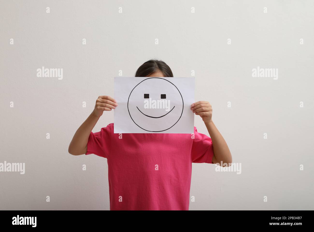 Little girl hiding behind sheet of paper with happy face on white ...