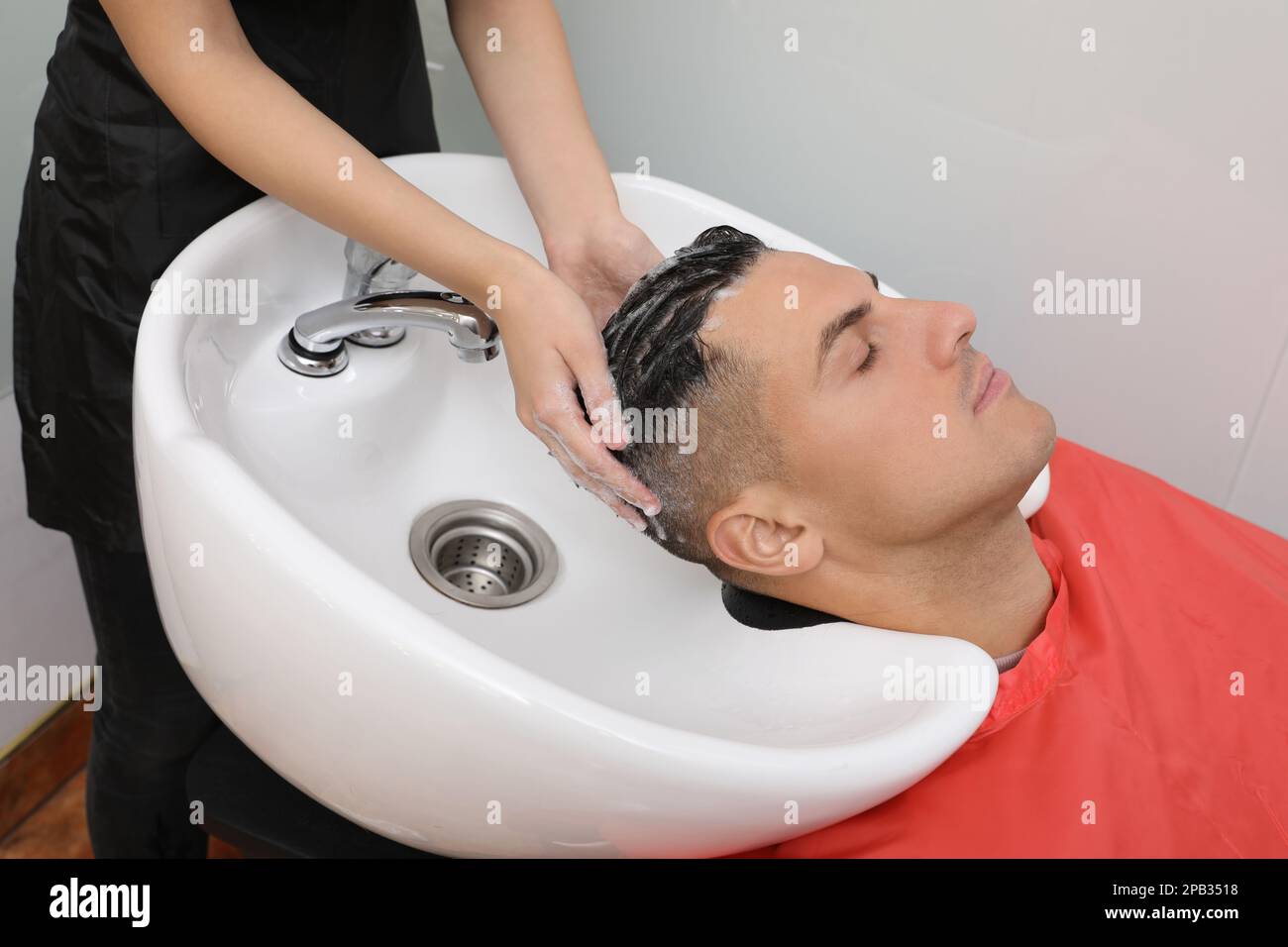 Professional hairdresser washing client's hair at sink in salon ...