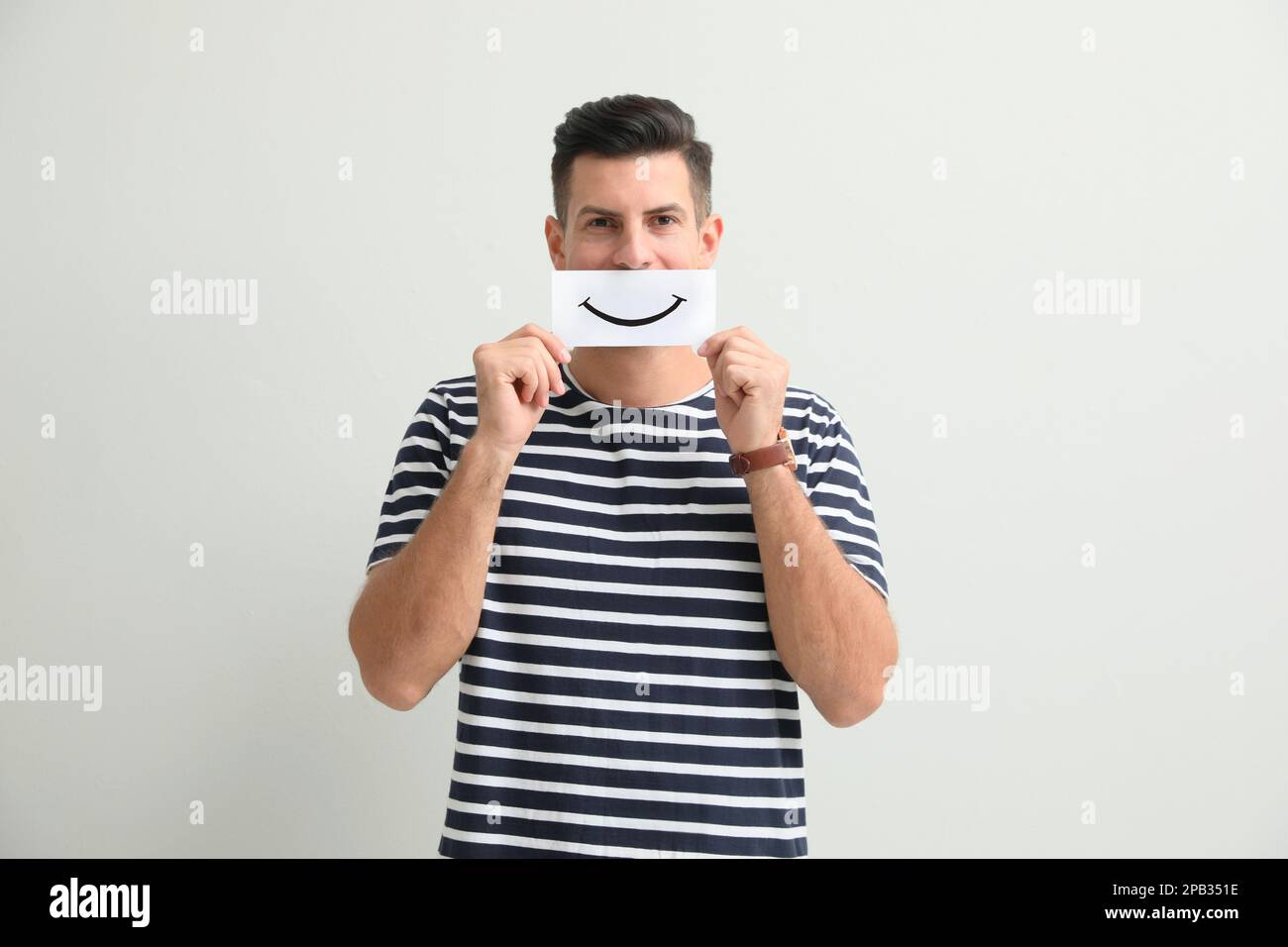 Man hiding emotions using card with drawn smile on white background ...