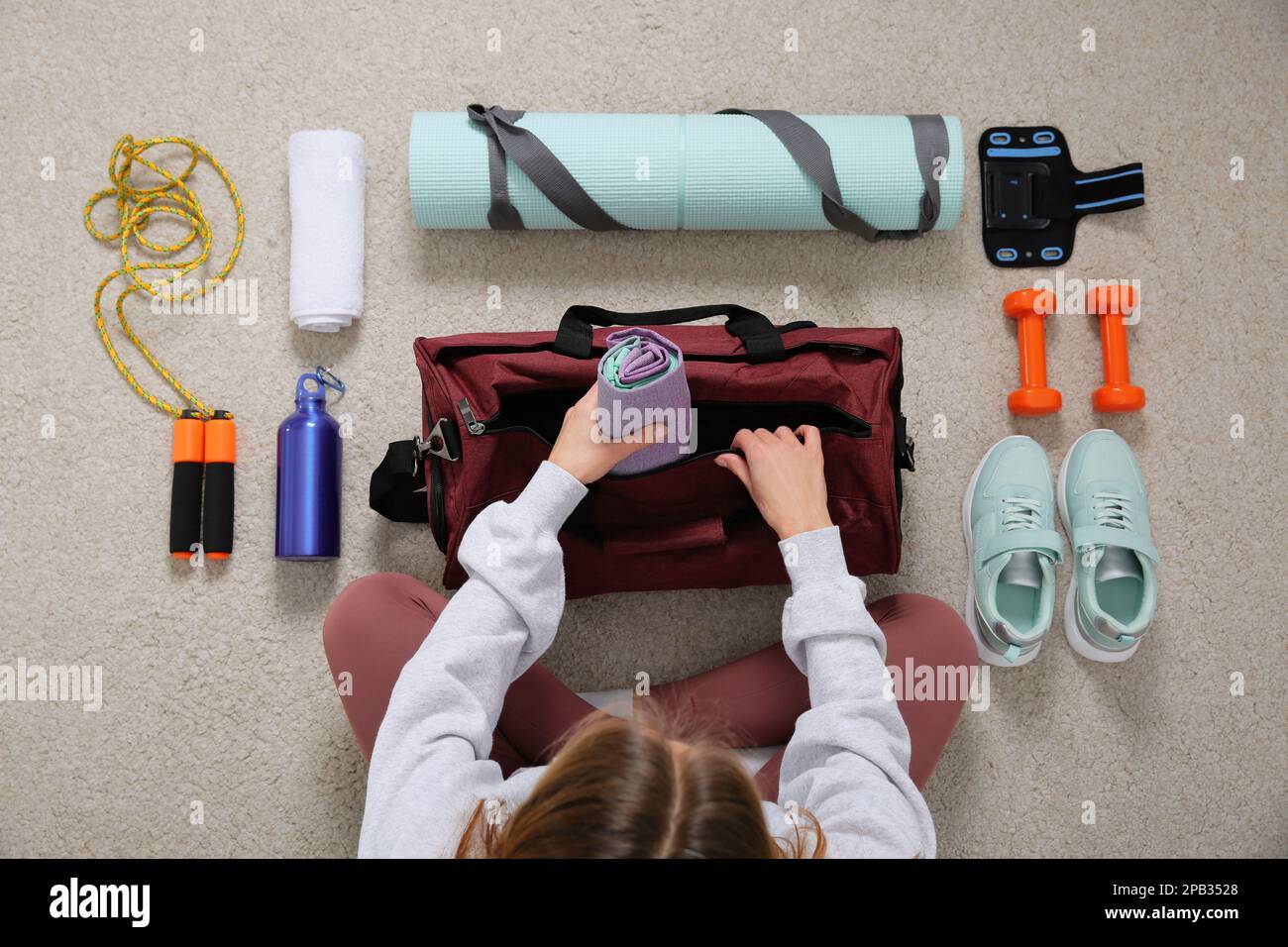 Woman packing sports stuff for training into bag on floor, top view ...