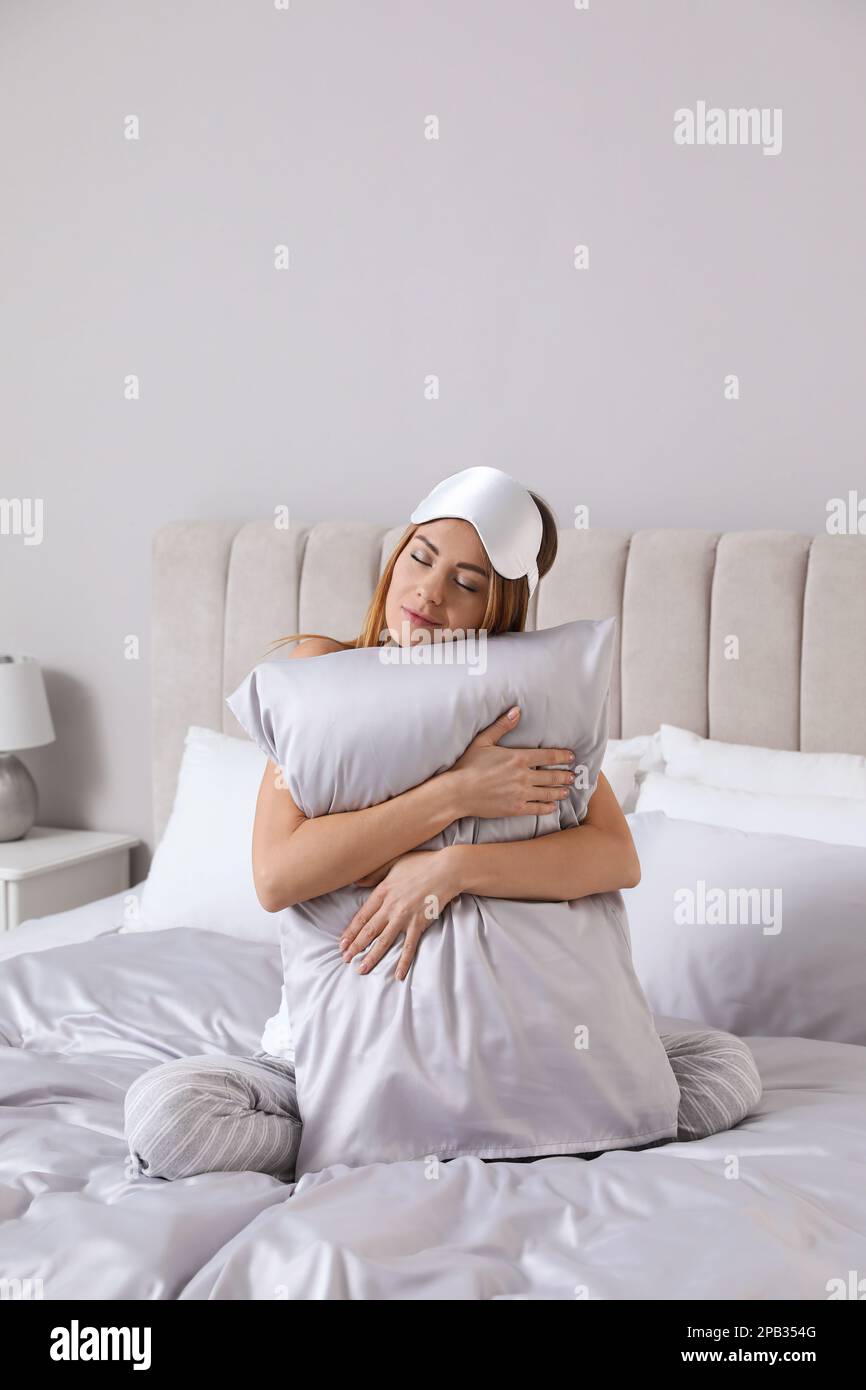 Beautiful woman hugging pillow on comfortable bed with silky linens ...