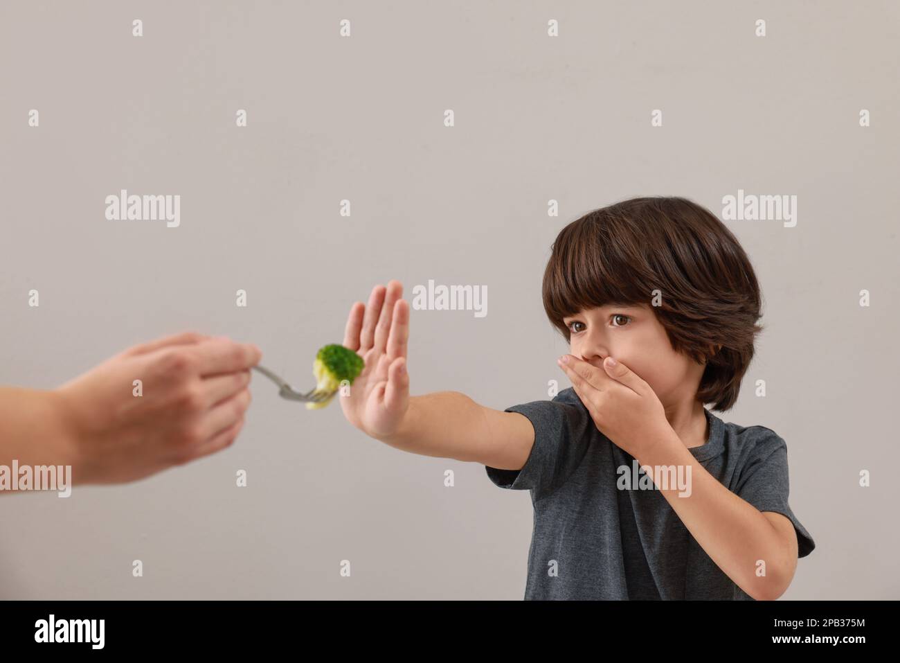 Cute little boy covering mouth and refusing to eat broccoli on grey ...